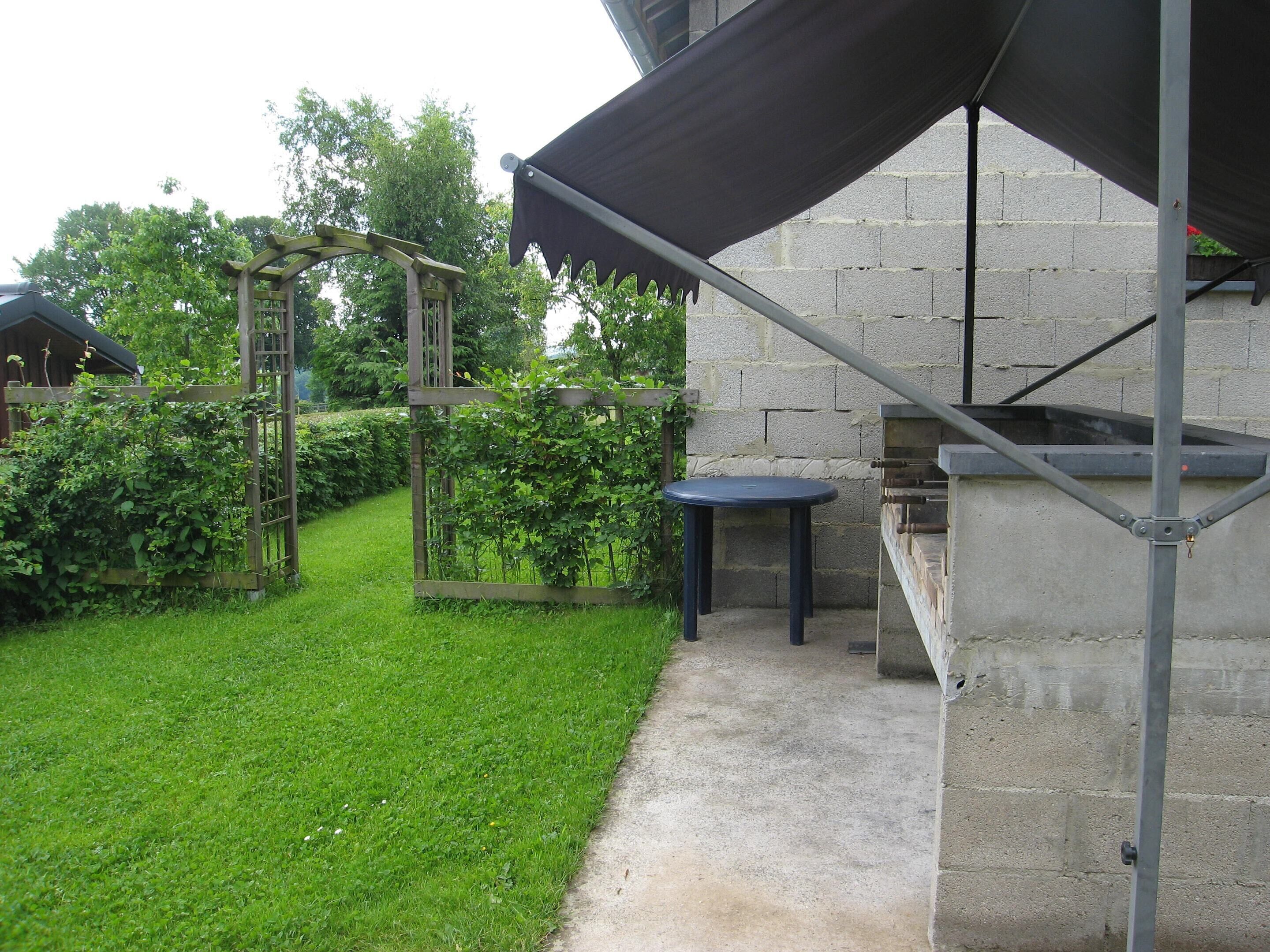Uma área de pátio com mesa, cadeiras, uma pérgola e um muro de tijolos.