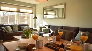Uma área de refeições com mesa de madeira posta para o café da manhã, incluindo pratos, copos e um vaso com flores.