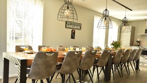 Uma área de refeições com uma mesa de madeira comprida, várias cadeiras e luminárias pendentes.