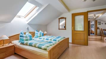 Quarto com teto inclinado, claraboia, cama de madeira, mesa de cabeceira, espelho e porta que dá para outro espaço.