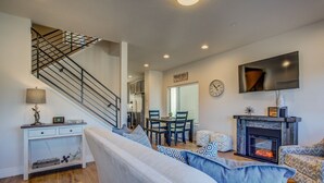 Uma sala de estar com escada, lareira, espaço de refeições e cozinha ao fundo.