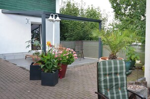 Uma área de pátio com plantas em vasos, uma cadeira de madeira e uma cadeira de metal.