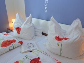 Quarto de hotel com cama, almofadas e um livro aberto.