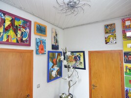 Quarto com porta de madeira, ventilador de teto e diversas obras de arte nas paredes.