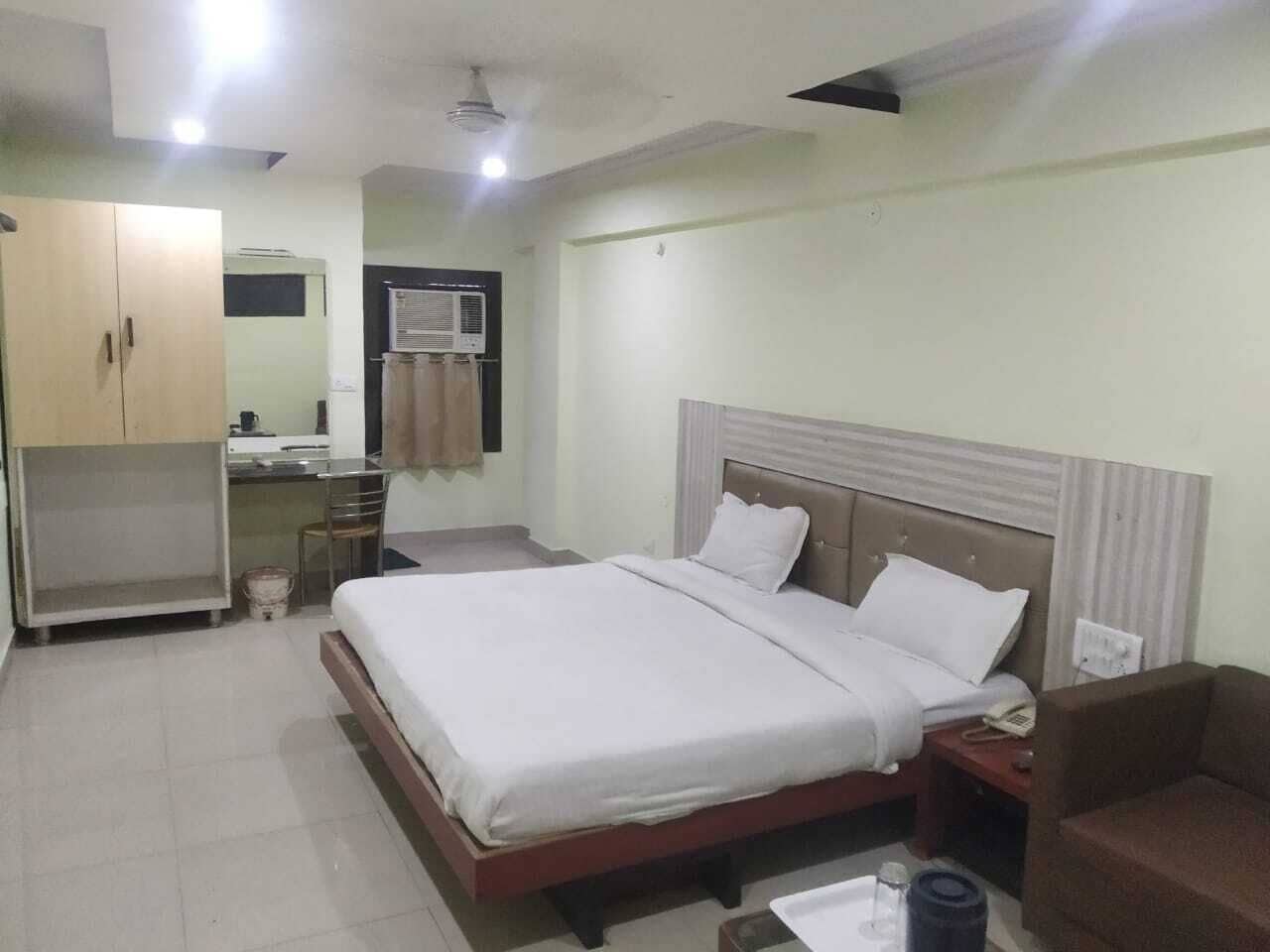 Quarto de hotel com cama, escrivaninha, cadeira, guarda-roupa e banheiro com ar condicionado.