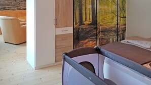 Um quarto moderno com um guarda-roupa, uma cama com colchão e almofadas, um sofá e uma parede com um mural de uma floresta.