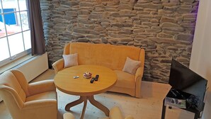 Uma sala de estar aconchegante com uma parede de pedra, uma mesa de madeira redonda e dois sofás bege.