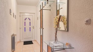 Um corredor com uma mesa de vidro exibindo um vaso de flores, um espelho e uma porta com detalhes em roxo.