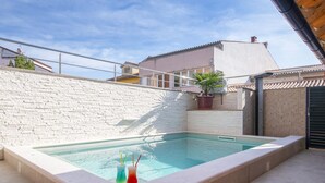 Piscina com parede de tijolos brancos e chão azulejado. Há duas bebidas na beira da piscina.