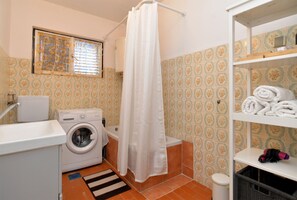 Casa de banho compacta com máquina de lavar roupa, cortina de chuveiro, sanita e uma prateleira com toalhas.