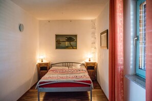 Quarto pequeno com uma cama, duas mesas de cabeceira com luminárias, um quadro na parede e uma janela com cortinas.
