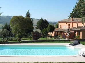 Piscina com vista para uma casa e colinas.