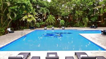 Piscina com espreguiçadeiras e mesas, cercada por vegetação exuberante.