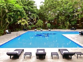 Piscina com espreguiçadeiras e mesas, cercada por vegetação exuberante.