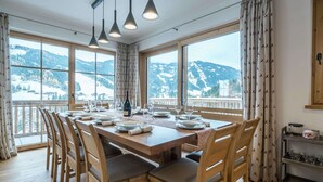 Uma sala de jantar com mesa de madeira posta para seis, janelas amplas com vista para as montanhas e luminárias pendentes.