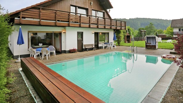 Uma casa de madeira de dois andares com piscina, área de estar externa e churrasqueira.