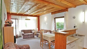 Um quarto aconchegante com teto de madeira, área de refeições, sofá, uma mesa pequena e cozinha com pia e armários.