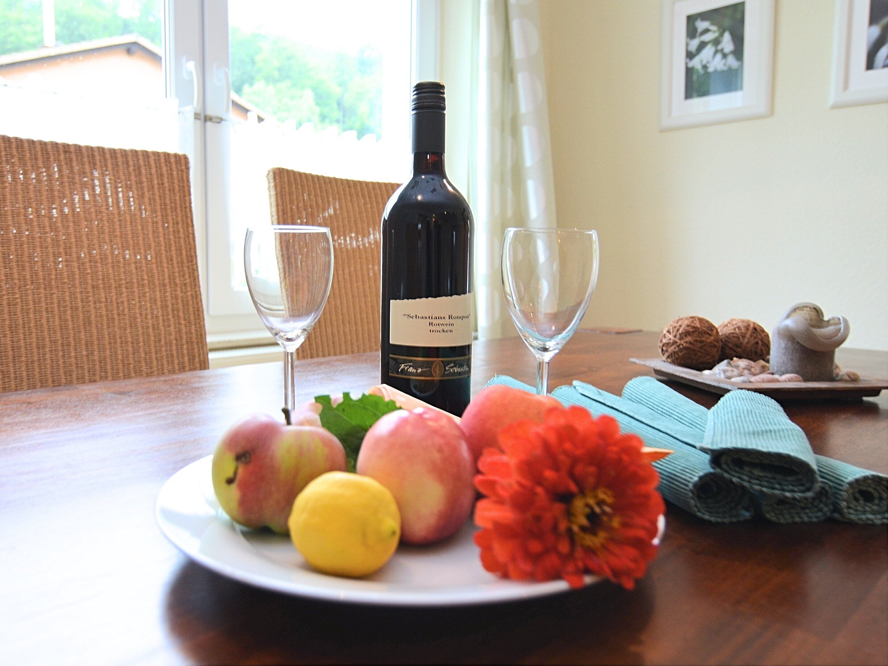 Uma mesa com uma travessa de frutas, uma garrafa de vinho e dois copos.
