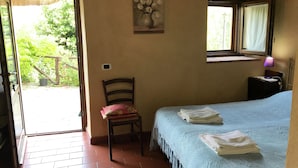 Quarto com cama, uma cadeira, uma janela e uma porta que dá para um jardim.