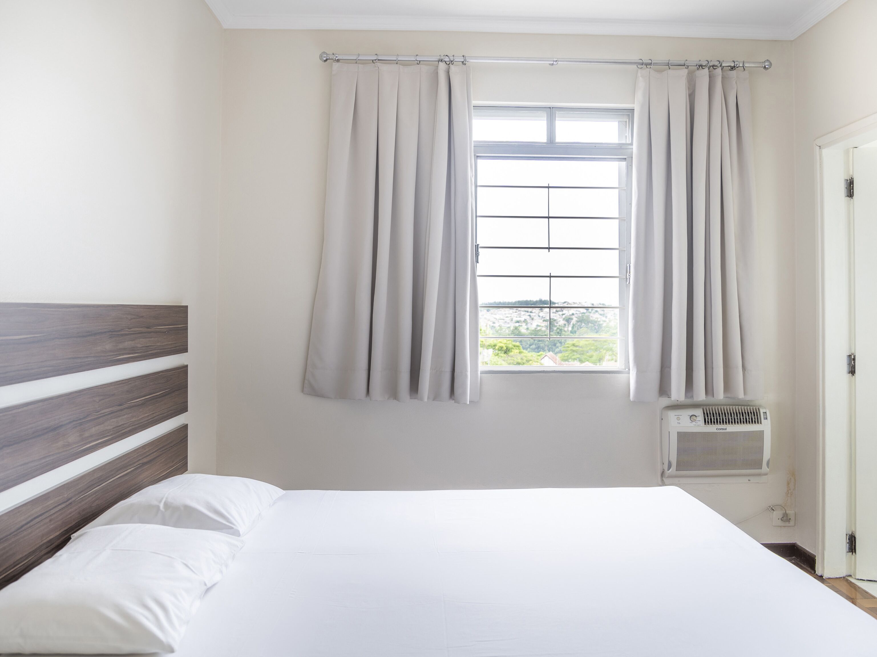 Quarto com cama, cortinas, janela com vista e ar condicionado.