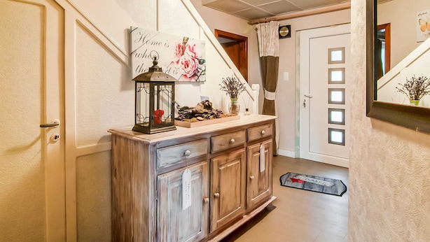 Um corredor com um armário de madeira, um candeeiro e uma porta com painel de vidro jateado.