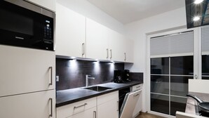 Cozinha moderna com armários brancos, bancada preta, micro-ondas Siemens, cafeteira e máquina de lavar loiça.