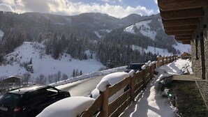 Uma estrada montanhosa coberta de neve, com uma cerca de madeira e um edifício à direita.