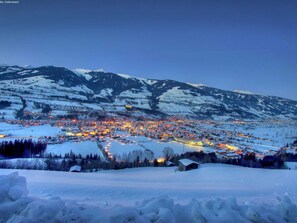 Uma cidade nas montanhas coberta de neve ao entardecer, com edifícios iluminados e uma vista ampla da paisagem circundante.