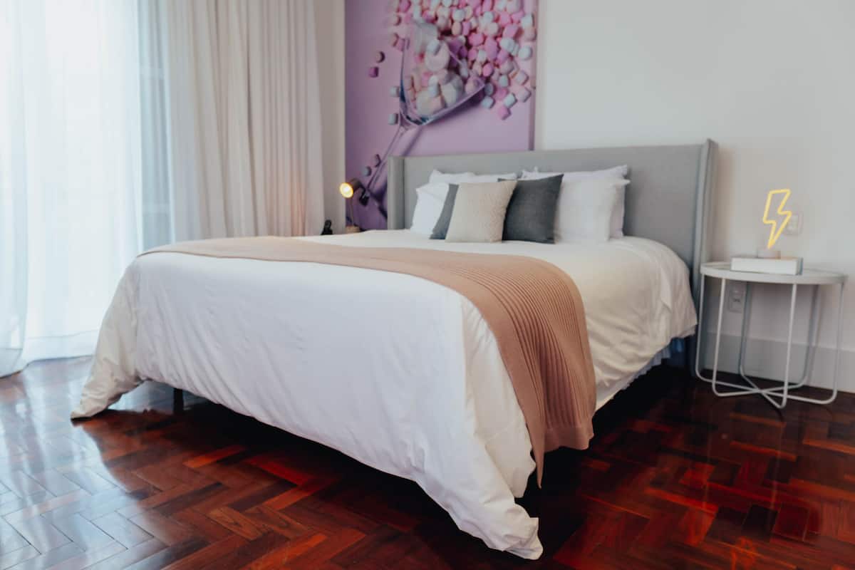Quarto moderno com uma cama grande, mesa de cabeceira com abajur e luminária na parede.