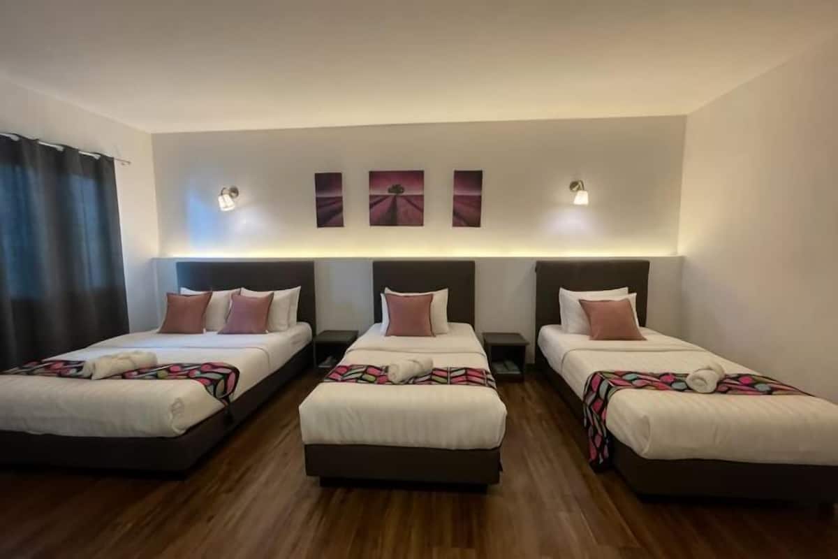 Quarto de hotel com três camas, piso de madeira e obras de arte penduradas na parede.