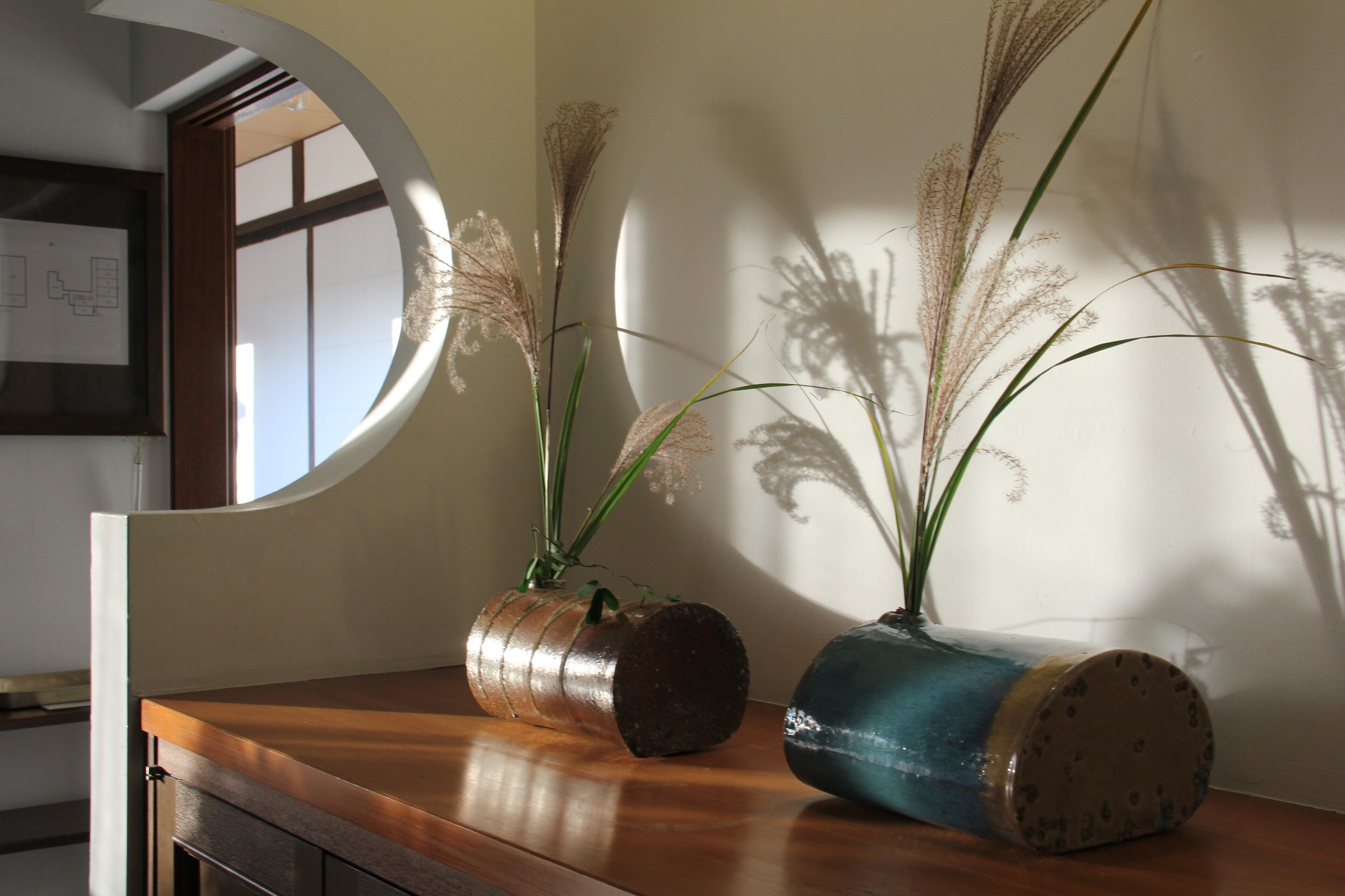Dois vasos cilíndricos com plantas sobre uma superfície de madeira.