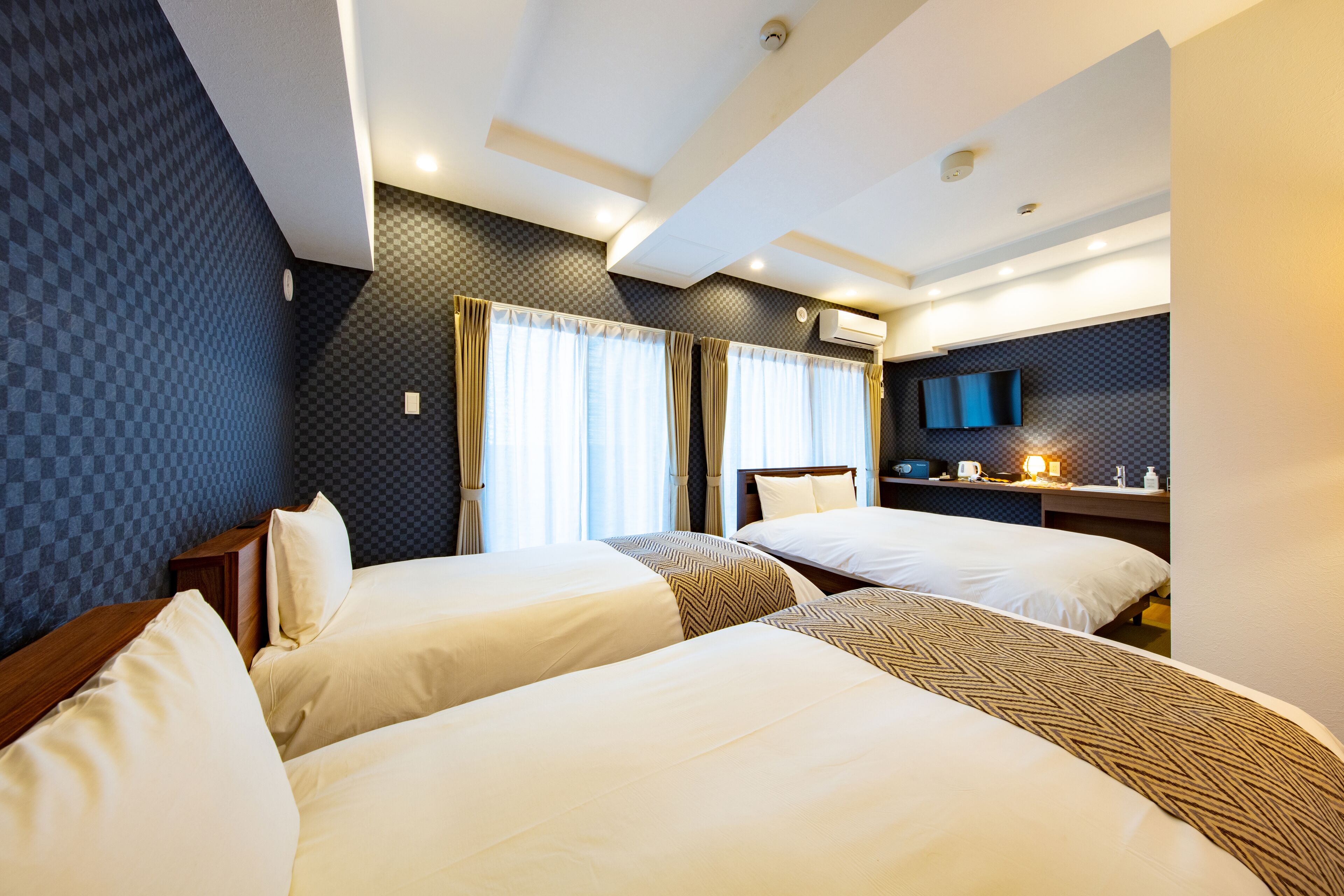 Quarto de hotel com duas camas, uma televisão de tela plana, uma mesinha de cabeceira e um aparelho de ar condicionado.