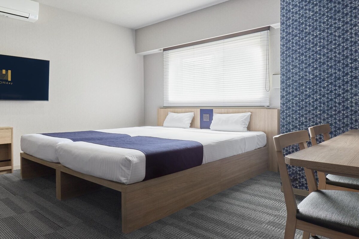 Quarto de hotel com uma cama, uma secretária e uma cadeira.