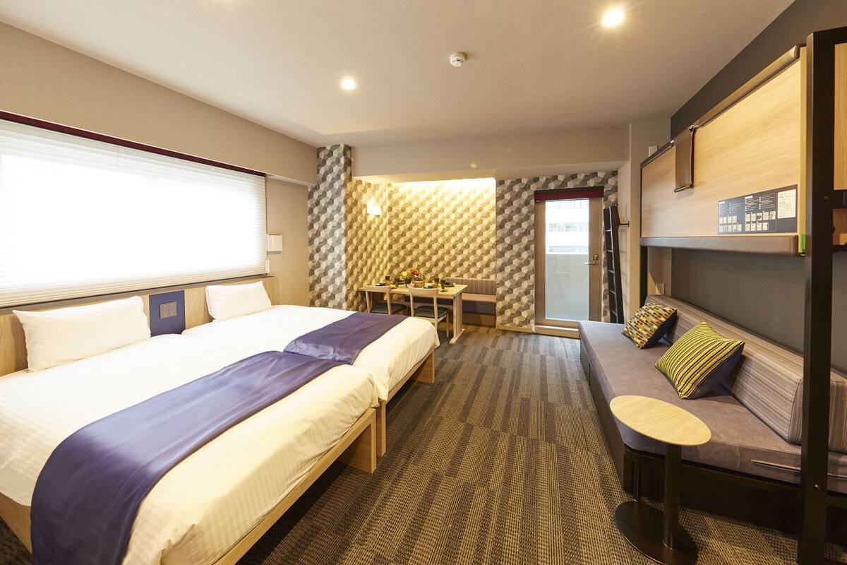 Quarto de hotel com duas camas, uma escrivaninha, um sofá e vista para a cidade.