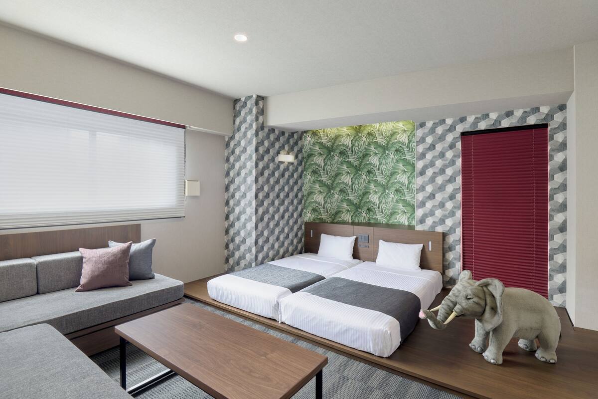 Quarto de hotel moderno com sofá, duas camas, uma decoração de elefante pequeno e paredes estampadas.