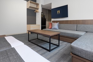 Quarto moderno com sofá, mesa de madeira, cabideiro suspenso e televisão na parede.