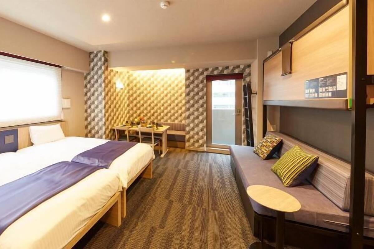 Quarto de hotel com cama, escrivaninha, área de estar e vista para o exterior.