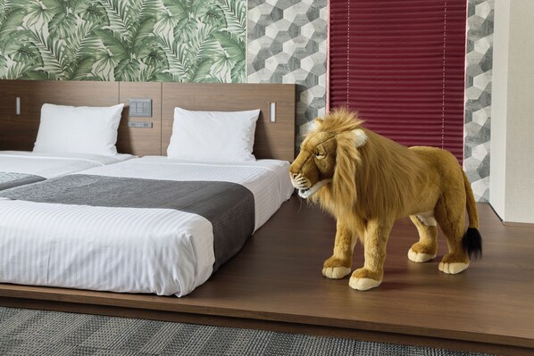 Quarto com cabeceira de madeira, duas almofadas brancas, um cobertor cinzento e uma estátua de leão no chão.