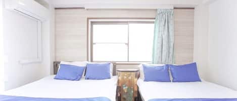Quarto de hotel com duas camas, uma janela com cortinas e uma mesinha entre as camas.