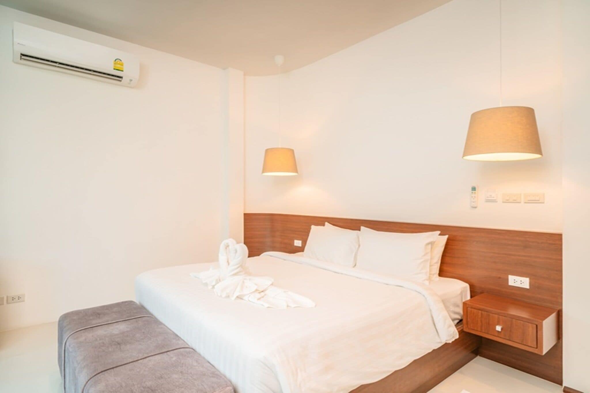 Quarto de hotel com uma cama, mesas de cabeceira, ar condicionado e duas luminárias fixadas na parede.