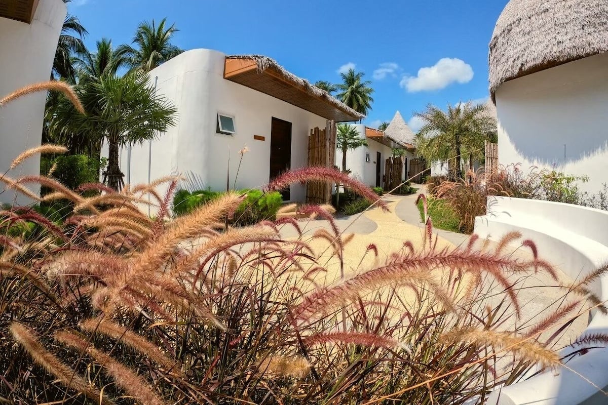 Resort com edifícios brancos, telhados de palha e palmeiras.