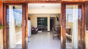 Ampla sala de estar com sofá, mesa de jantar e cadeiras. Há uma porta de vidro deslizante que dá para uma área externa.