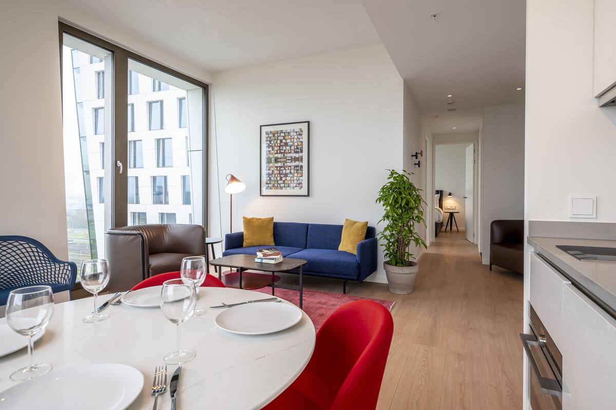 Uma sala de estar moderna com uma mesa de jantar para quatro pessoas, um sofá azul e uma janela grande com vista para a cidade.