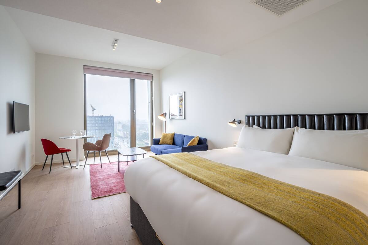 Quarto de hotel moderno com uma cama grande, um sofá, uma mesa e uma cadeira.
