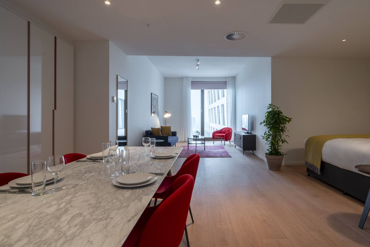Quarto de hotel moderno com área de refeições, cama, televisão e planta.