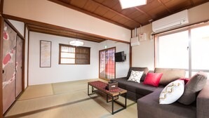 Um quarto japonês tradicional com tatames, um sofá com almofadas, uma mesinha e uma porta deslizante com vista.