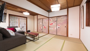 Um quarto japonês tradicional com tatames, um sofá com almofadas, uma mesinha baixa e portas deslizantes com arte.