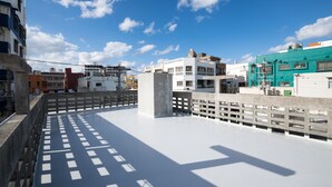 Terraço no telhado com piso de concreto, grades e vista dos edifícios ao redor.