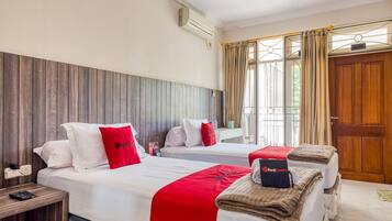 Quarto de hotel com duas camas, cabeceira de madeira, janela com cortinas e uma porta.