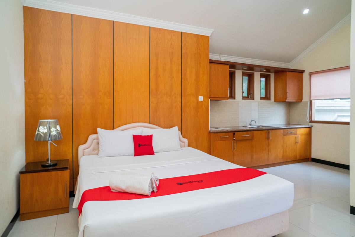 Quarto de hotel com uma cama grande, guarda-roupa de madeira, mesa de cabeceira pequena com abajur e área de kitchenette.
